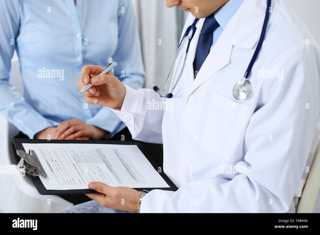 Male doctor holding application form while consulting female patient in ...