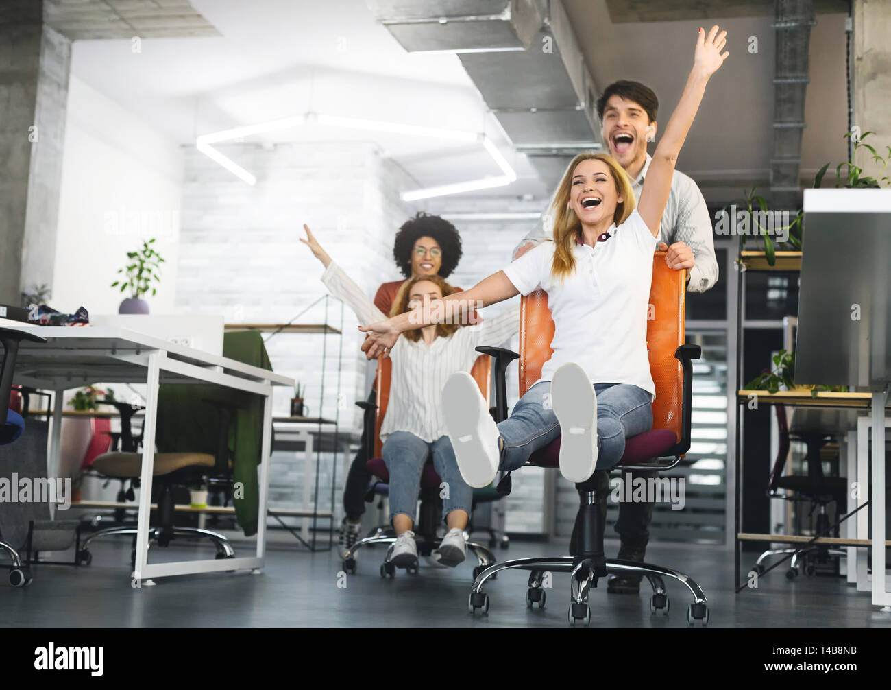Group of young coworkers enjoying chair race at work Stock Photo - Alamy