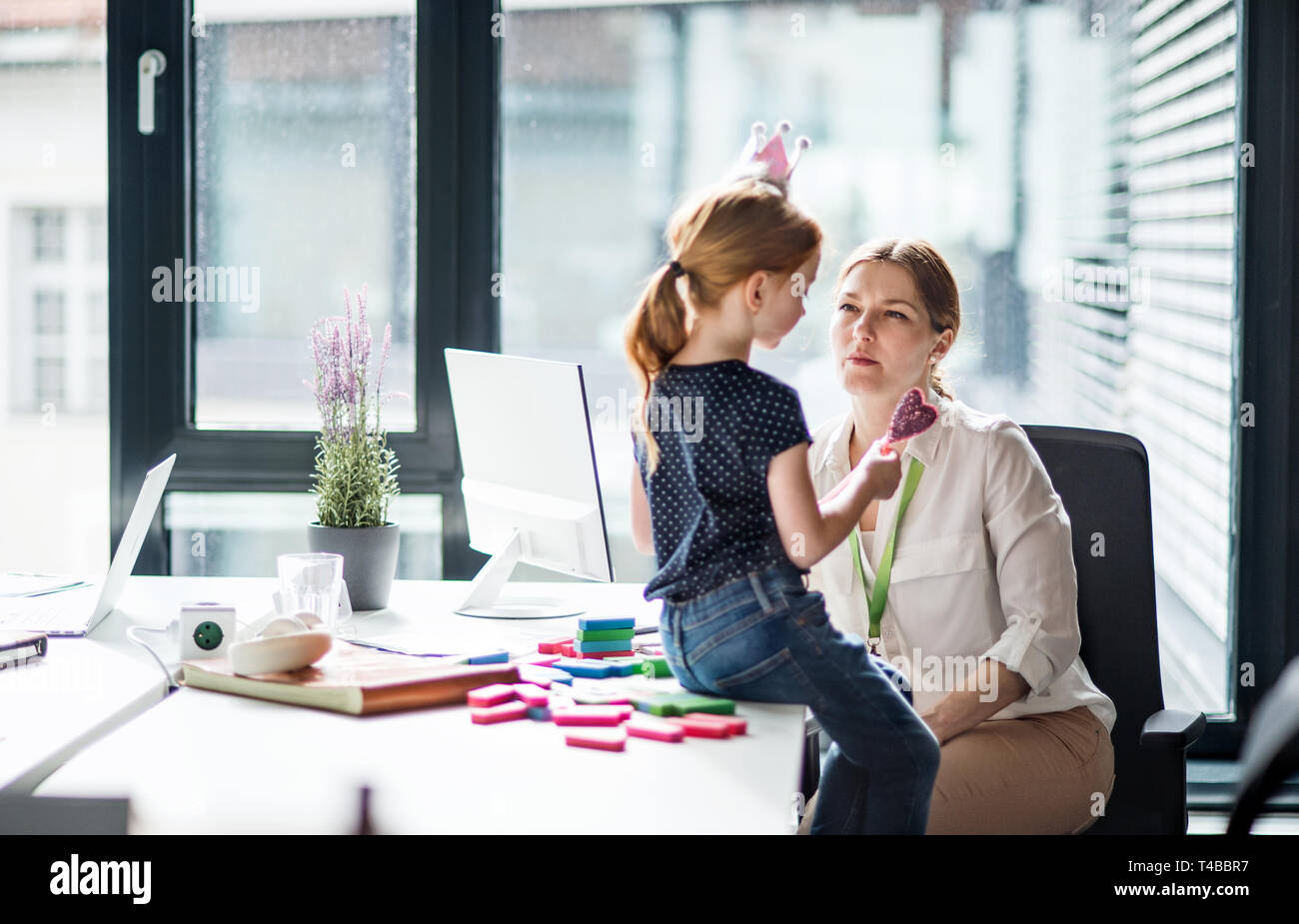 A businesswoman with small daughter sitting in an office, working Stock ...