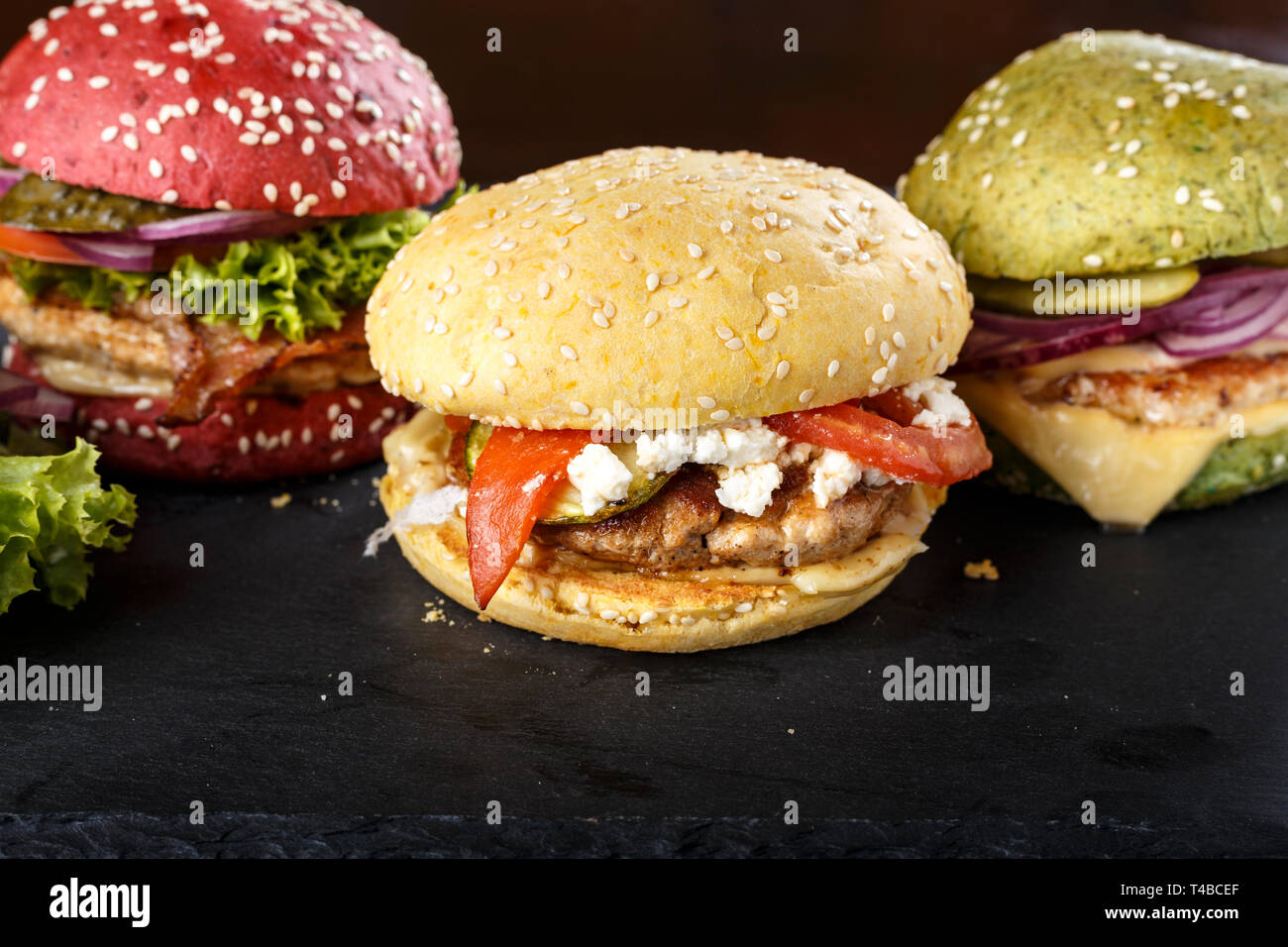 burgers with multi-colored buns on a black table. clearly visible ...