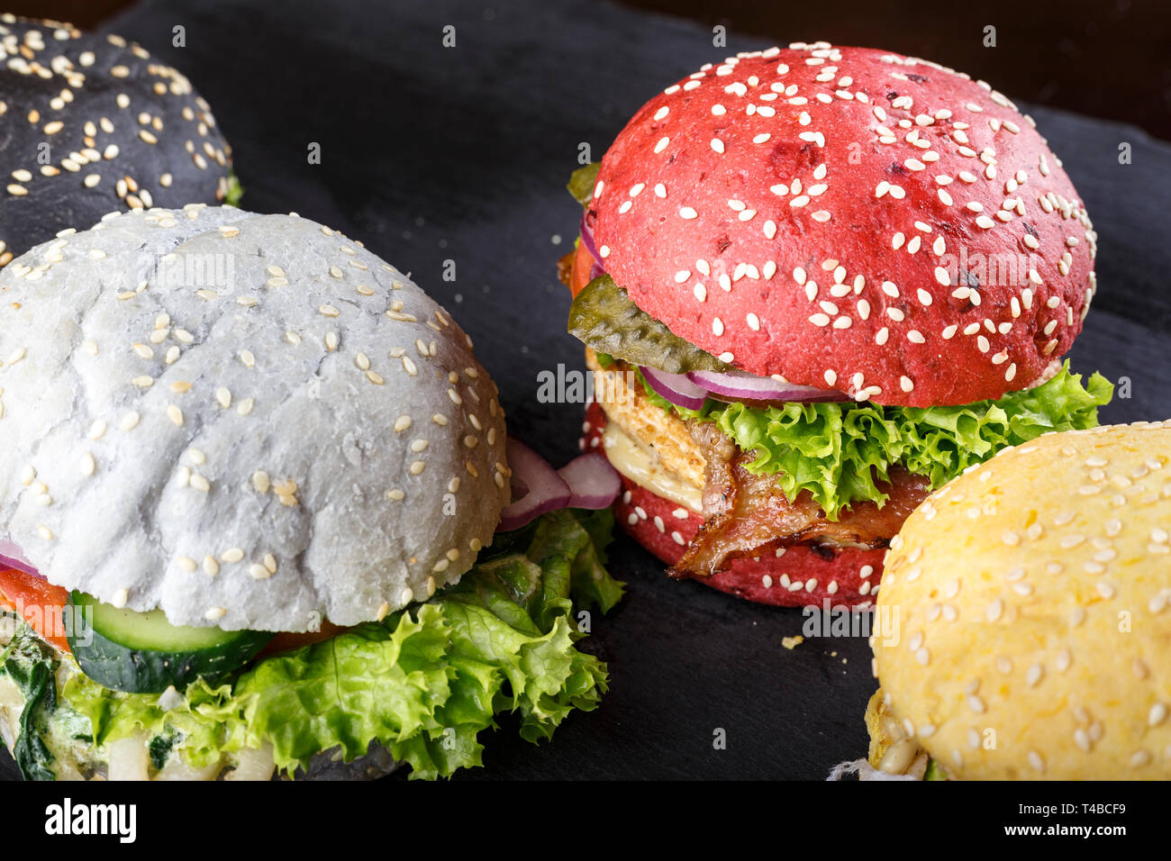 burgers with multi-colored buns on a black table. clearly visible ...