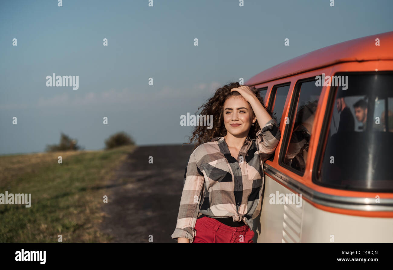 A young girl on a roadtrip through countryside, leaning on a minivan ...