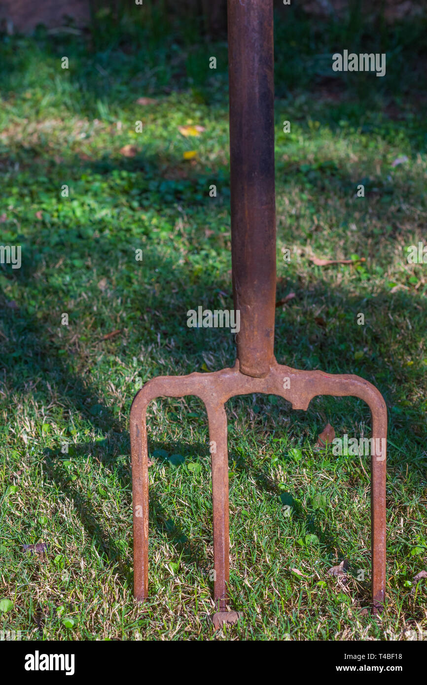 Old rusted garden fork with a missing tine isolated against a green ...