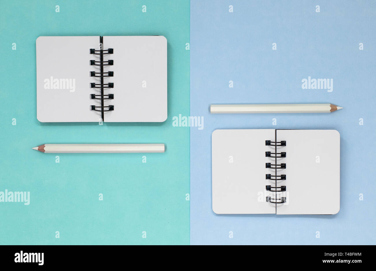 Two open spiral notebooks with white pencils, on a blue green ...