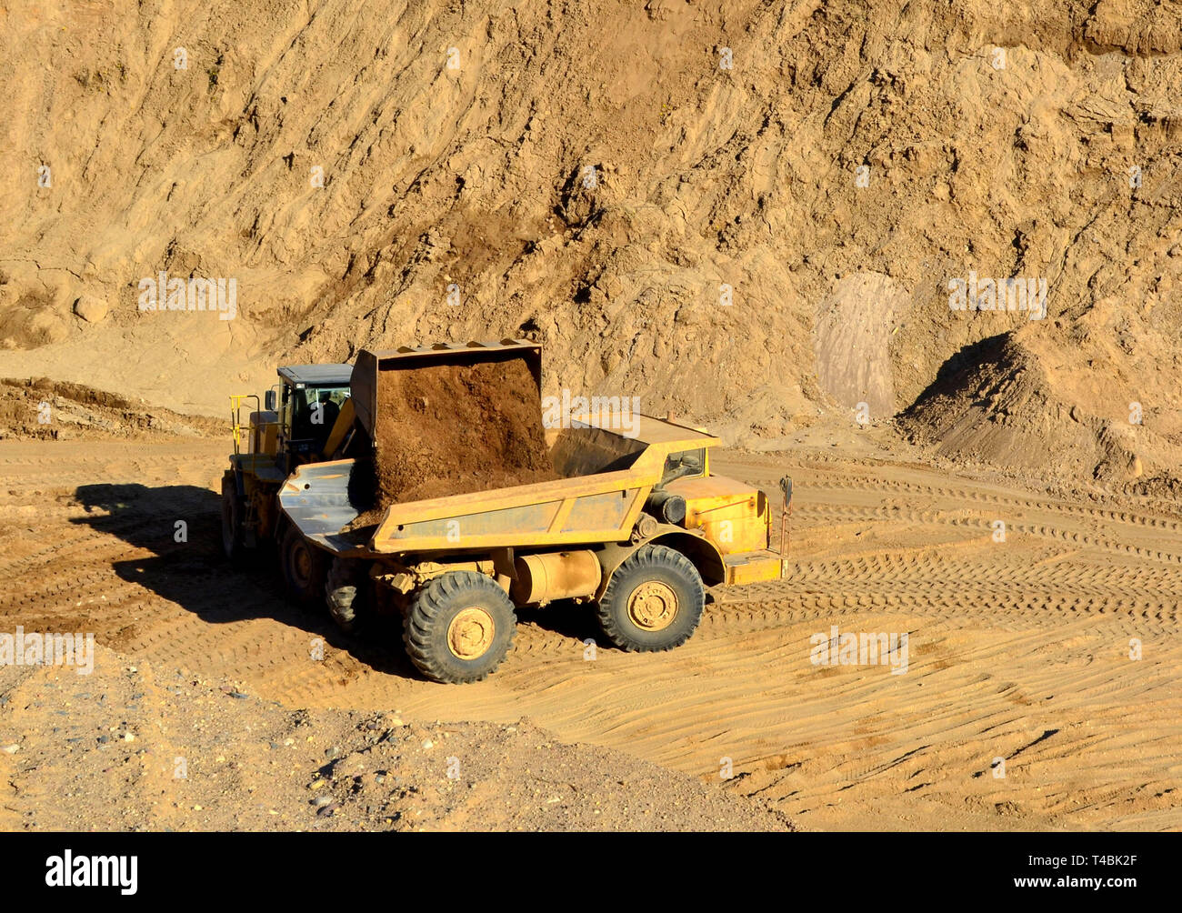Front-end loader loading with sand a heavy dump truck in a mining ...
