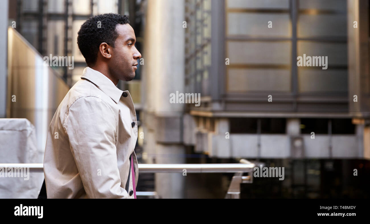 Waist up side view of young black businessman walking past modern ...