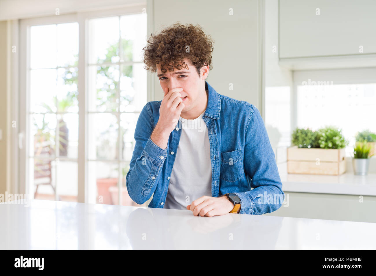 Young handsome man wearing casual denim jacket at home smelling ...
