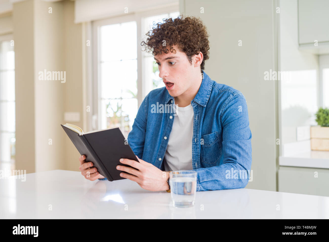 Young man reading a book at home scared in shock with a surprise face ...