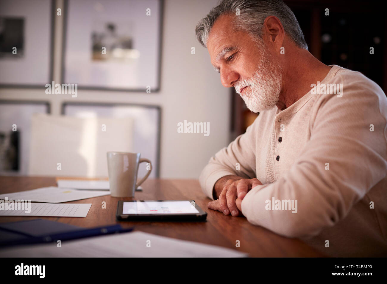 Senior Hispanic man sitting at a table using a tablet computer in the ...