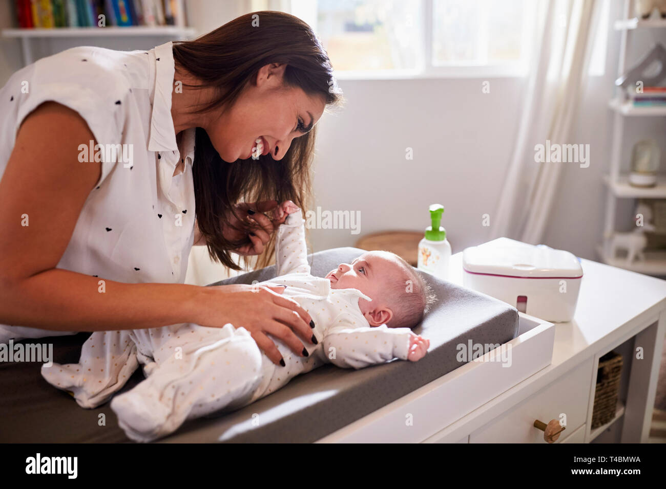 Happy mother changing the diaper of her baby at home on a changing ...