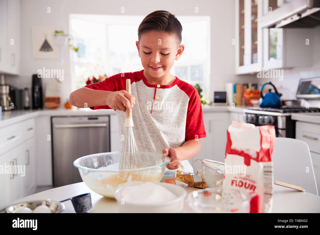 Pre-teen boy making a cake in the kitchen mixing cake mix, smiling ...