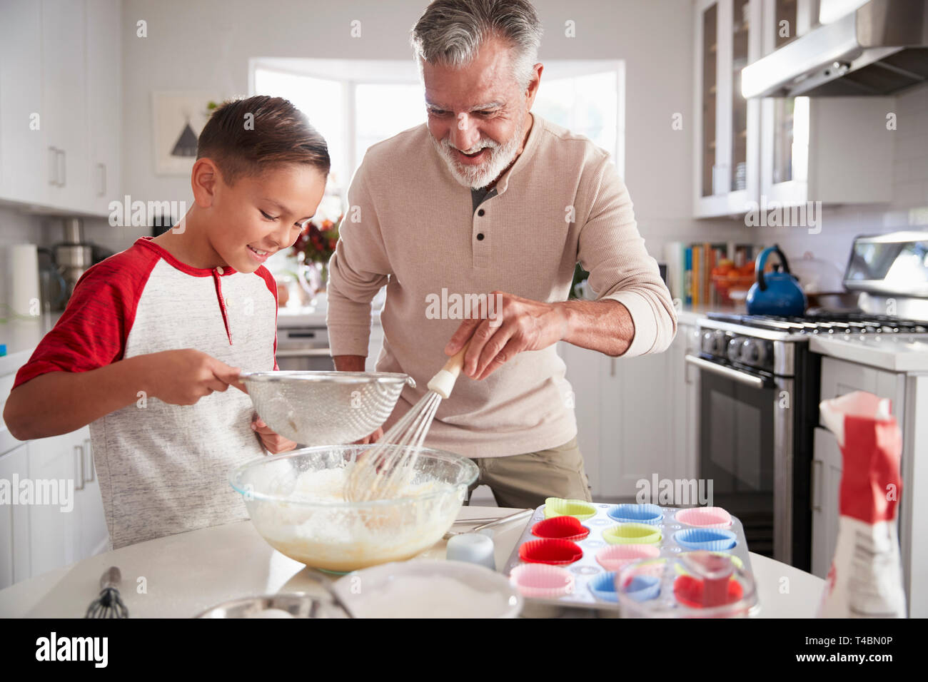 Pre-teen boy making cake mixture in the kitchen with his grandfather ...