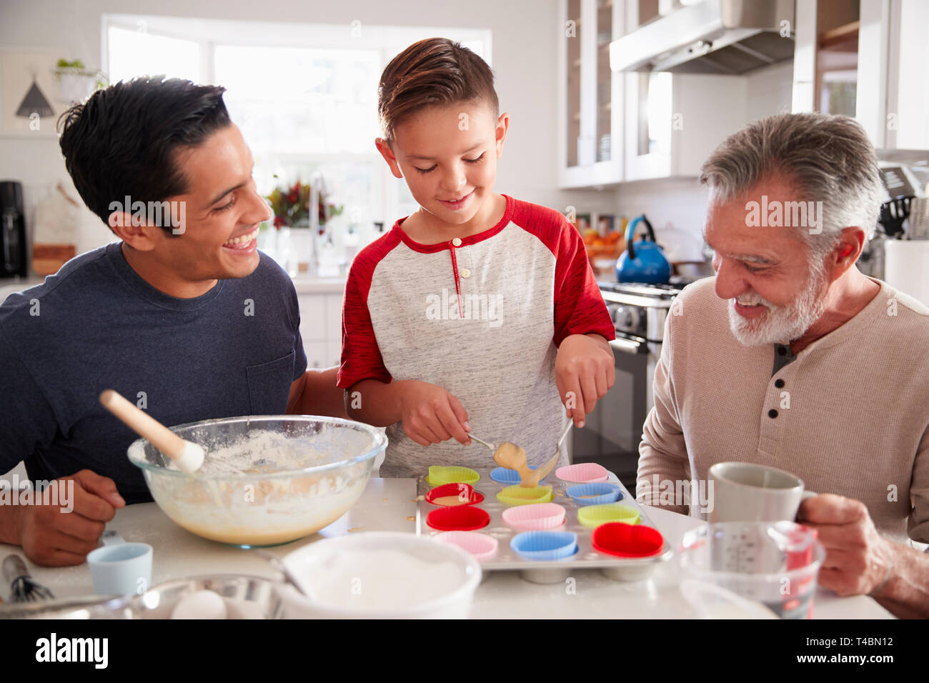 Three male generations of family making cakes together at the table in ...