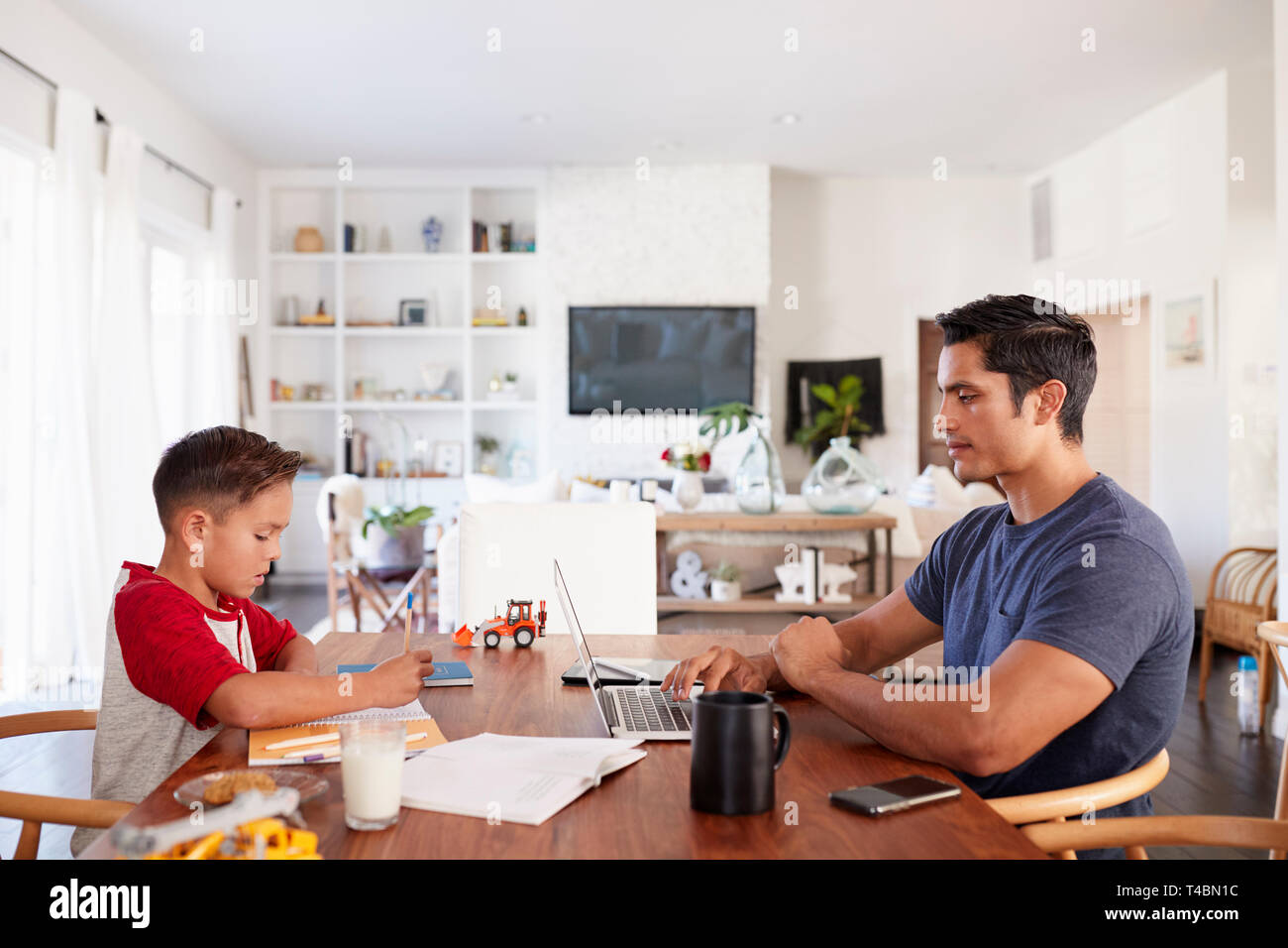 Hispanic father and son working opposite each other at the dining room ...