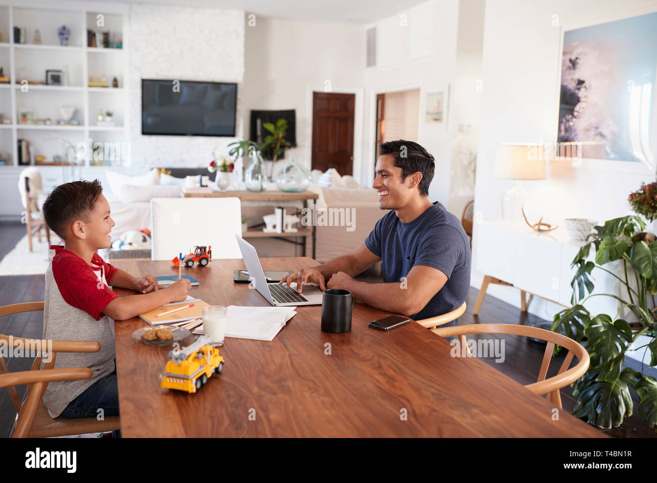 Hispanic father and son working at opposite sides of the dining room ...