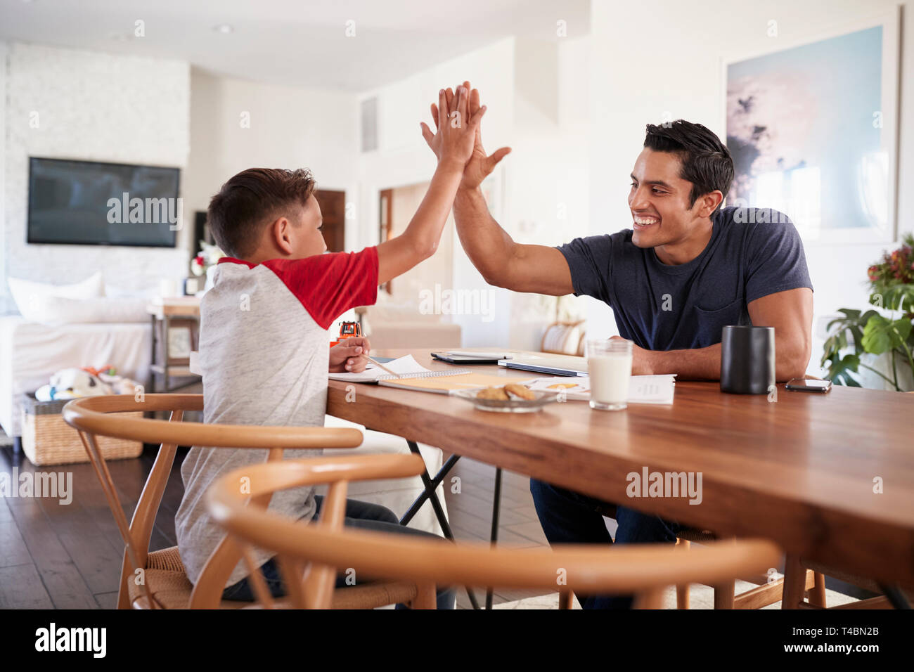 Hispanic father and son sitting opposite each other, high five over the ...