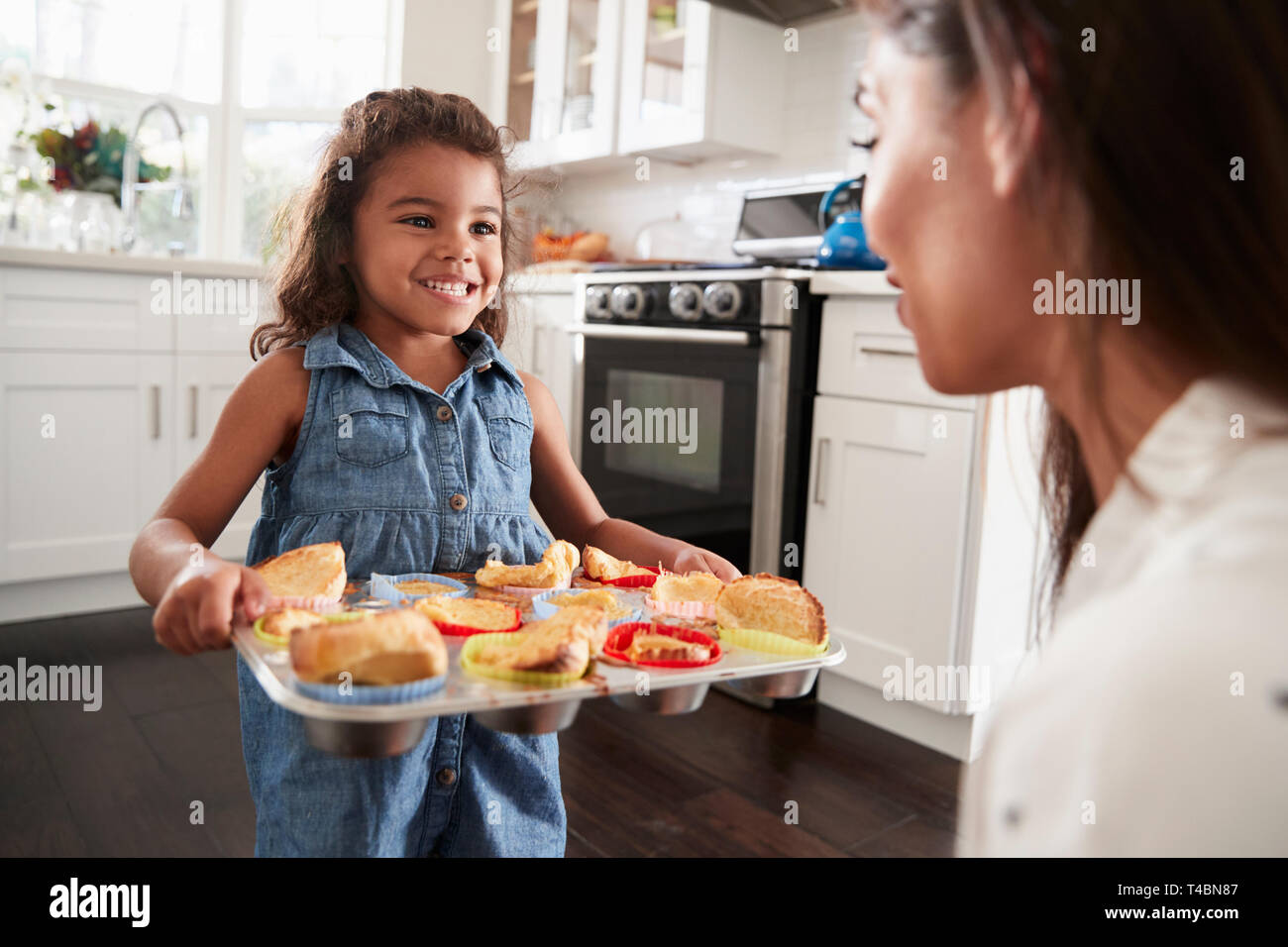 Smiling young Hispanic girl standing in kitchen presenting the cakes ...