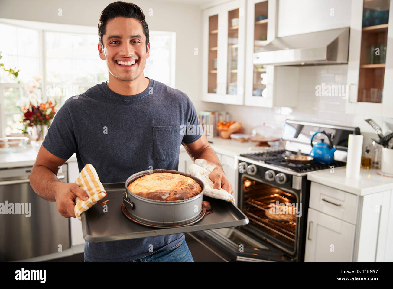 Smiling millennial Hispanic man standing in kitchen presenting the cake ...