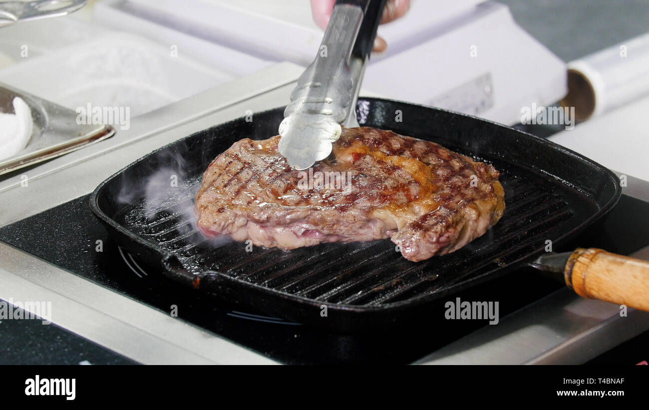 Restaurant kitchen. Frying a steak in the pan. A chef about to turn the ...