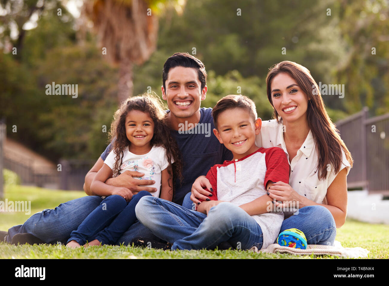 Happy young Hispanic family sitting the on grass in the park smiling to ...