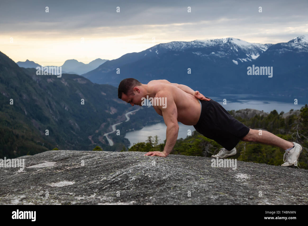 Fit and Muscular Young Man is doing exercises on top of the Mountain ...