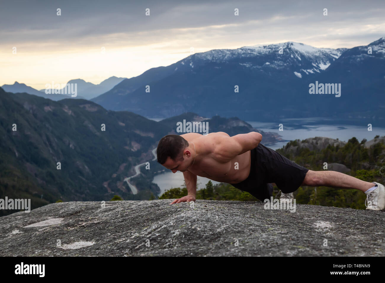 Fit and Muscular Young Man is doing exercises on top of the Mountain ...