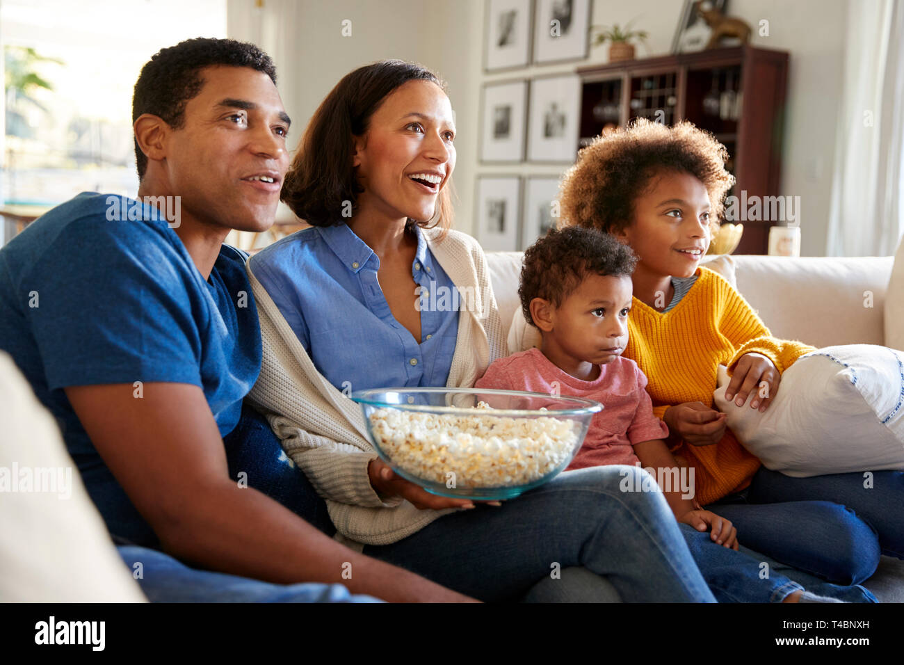 Young family sitting together on the sofa in their living room watching ...