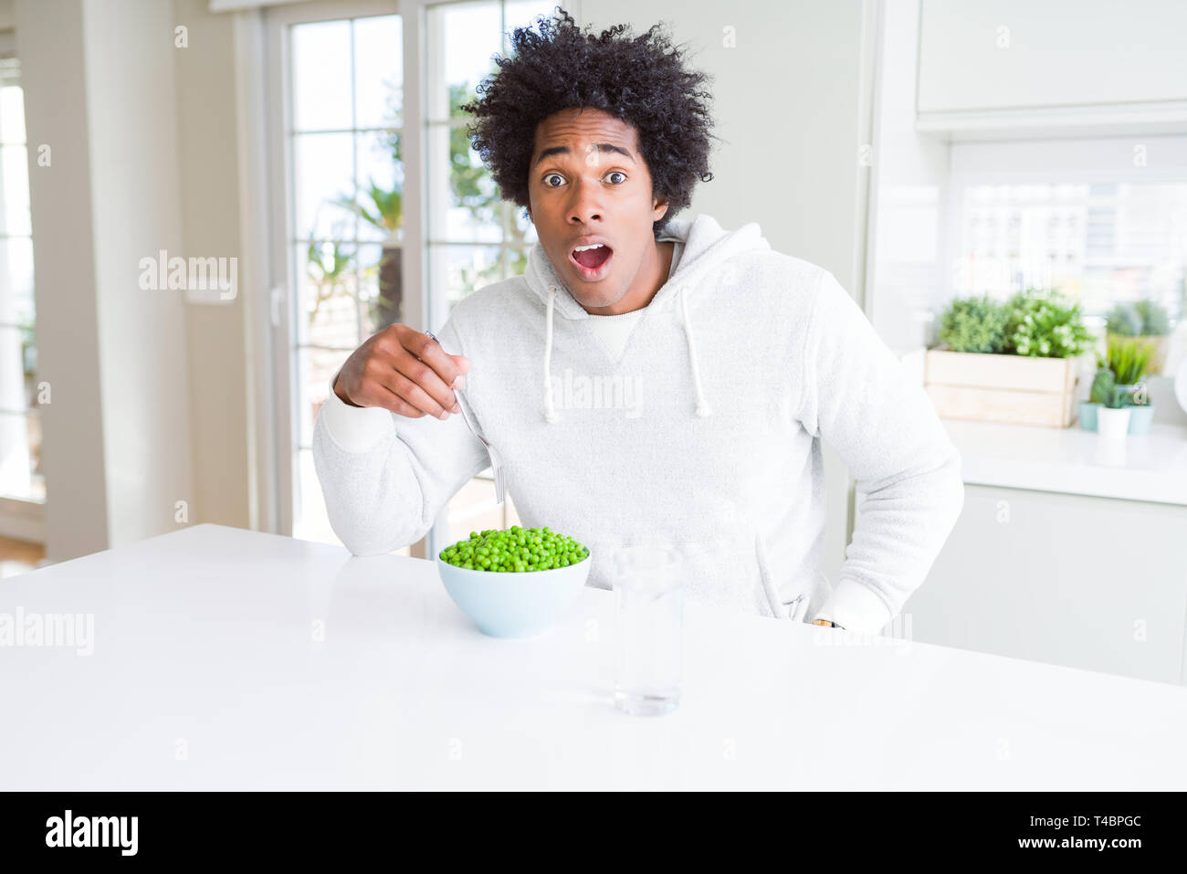 African American man eating fresh green peas at home scared in shock ...