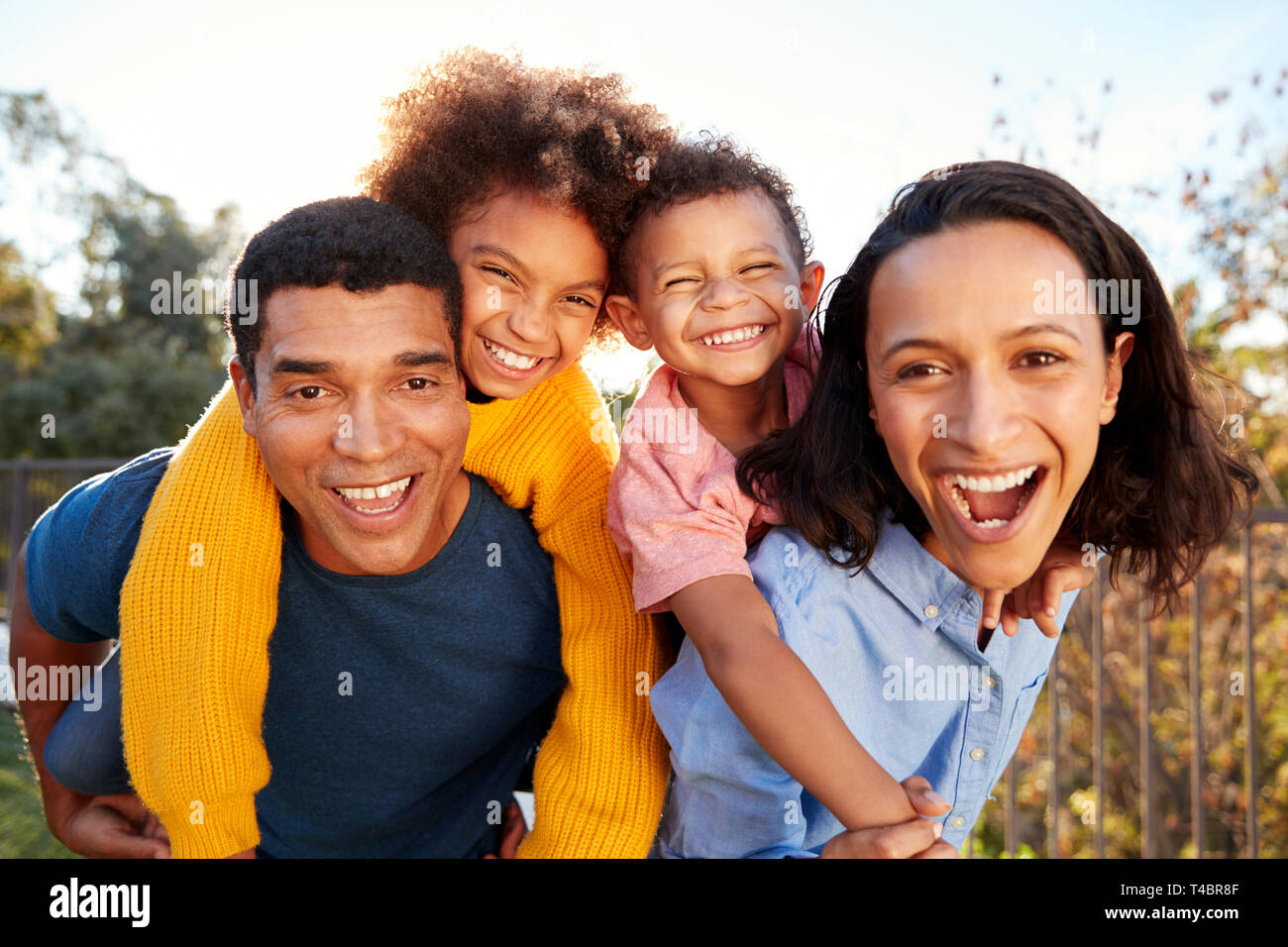 Young mixed race parents parents having fun piggybacking their children ...