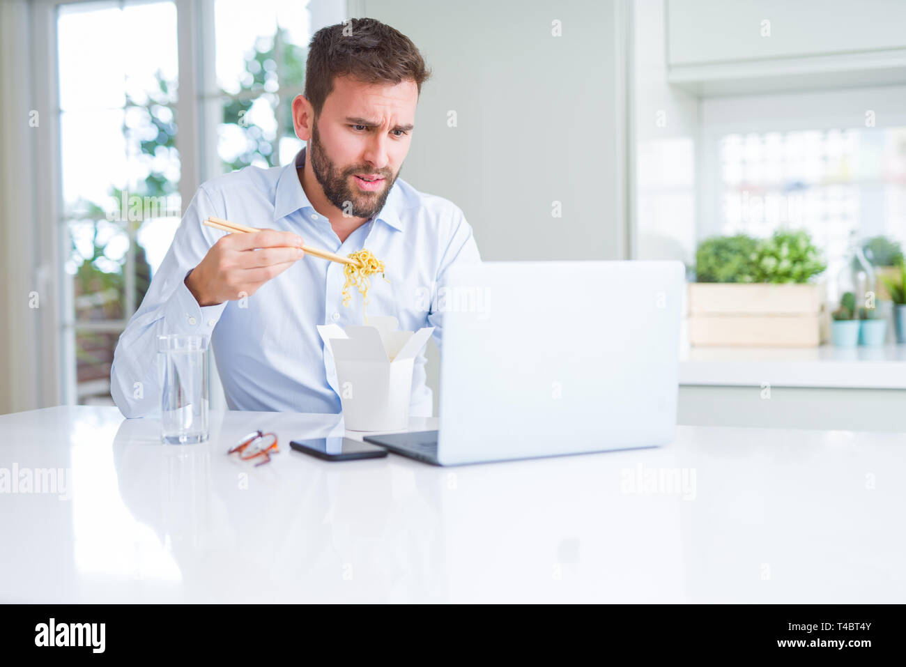 Business man eating take away asian noodles food while working using ...
