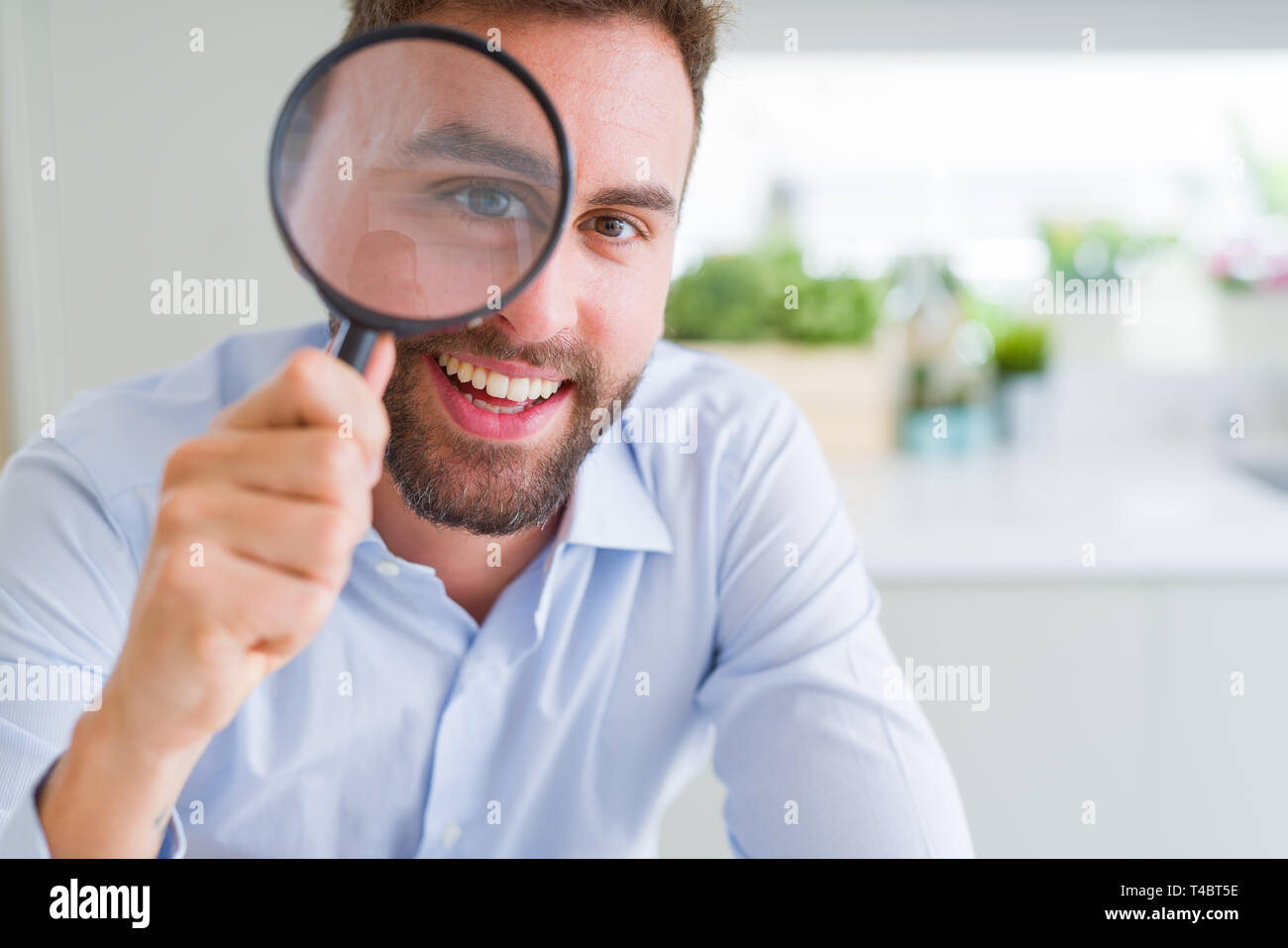 Handsome business man holding magnifying glass close to face, big eyes ...