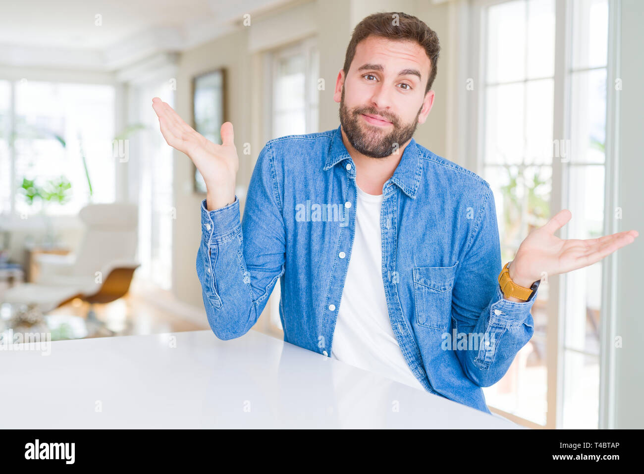 Handsome man at home clueless and confused expression with arms and ...