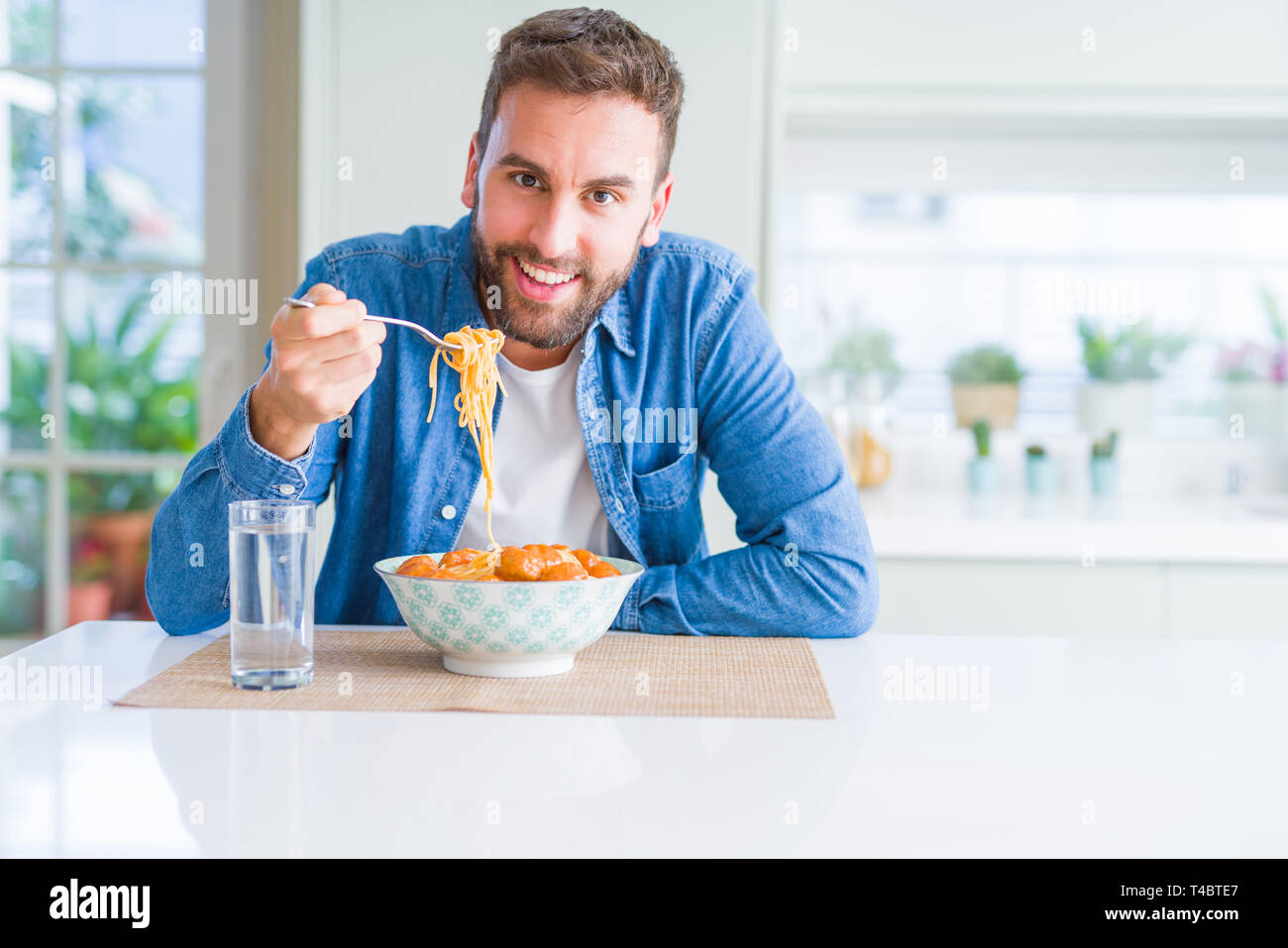 Handsome man eating pasta with meatballs and tomato sauce at home while ...