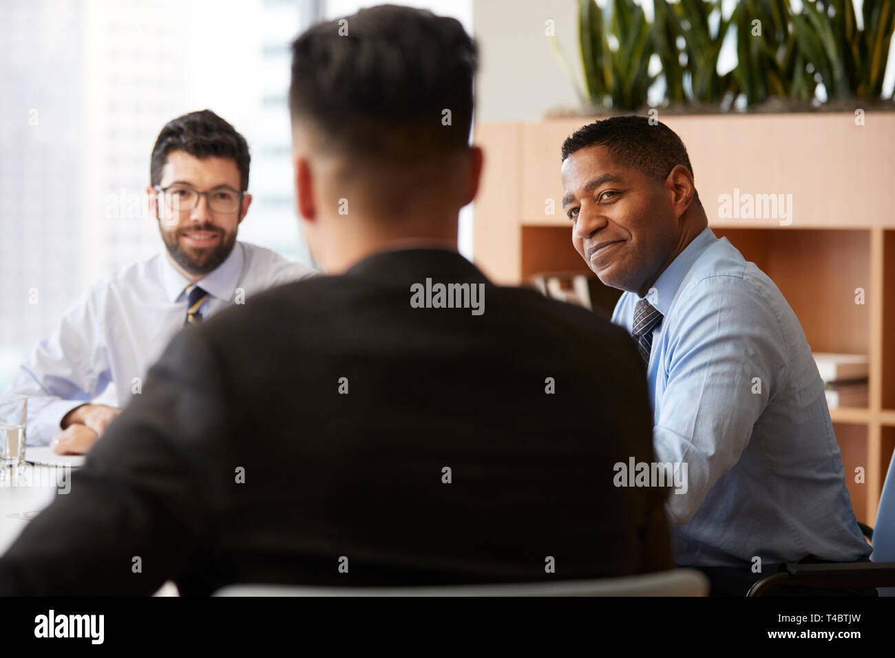 Three Businessmen Sitting Around Table Meeting In Modern Open Plan ...