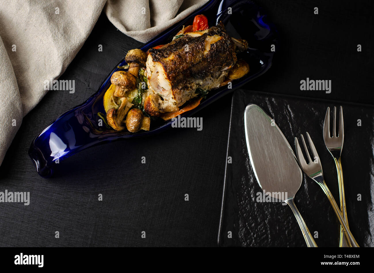 Roasted hake fish with vegetables on a blue plate on black background ...