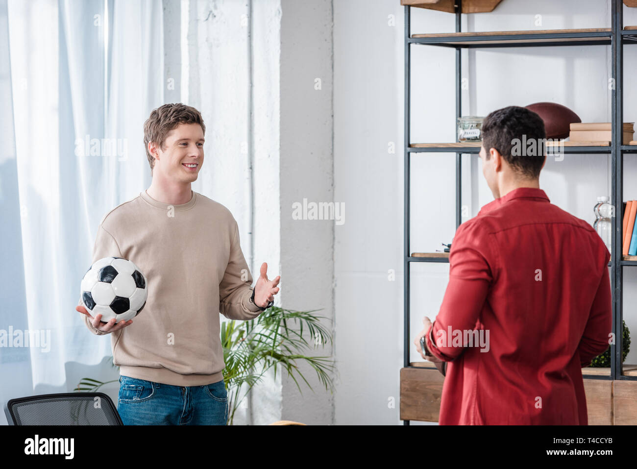 Two friends with football ball talking with smile at home Stock Photo ...