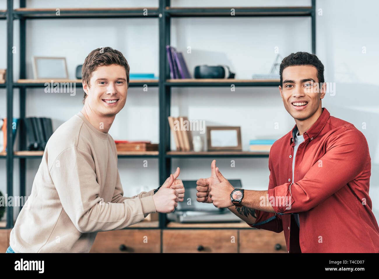 Two smiling multiethnic friends showing thumbs up and looking at camera ...