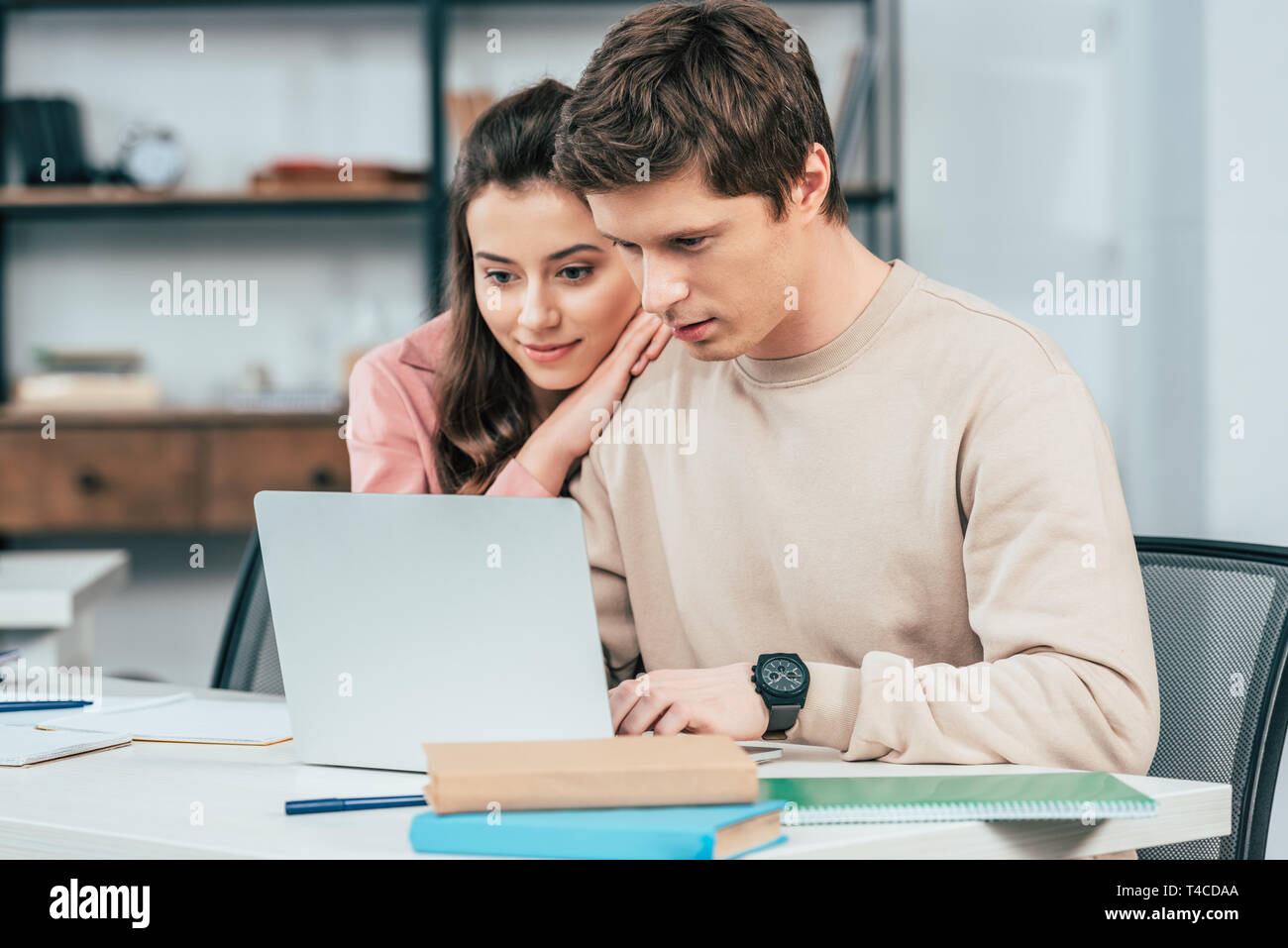 Smiling students sitting at desks and using laptop while studying in ...