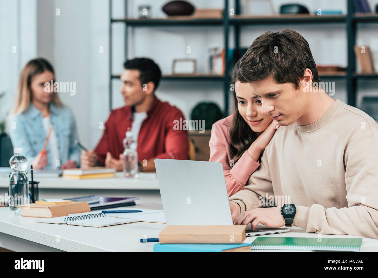 Smiling students sitting at desks and using laptop while studying in ...