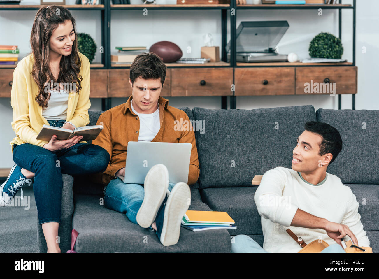 Three multiethnic students with notebooks and laptop studying while ...