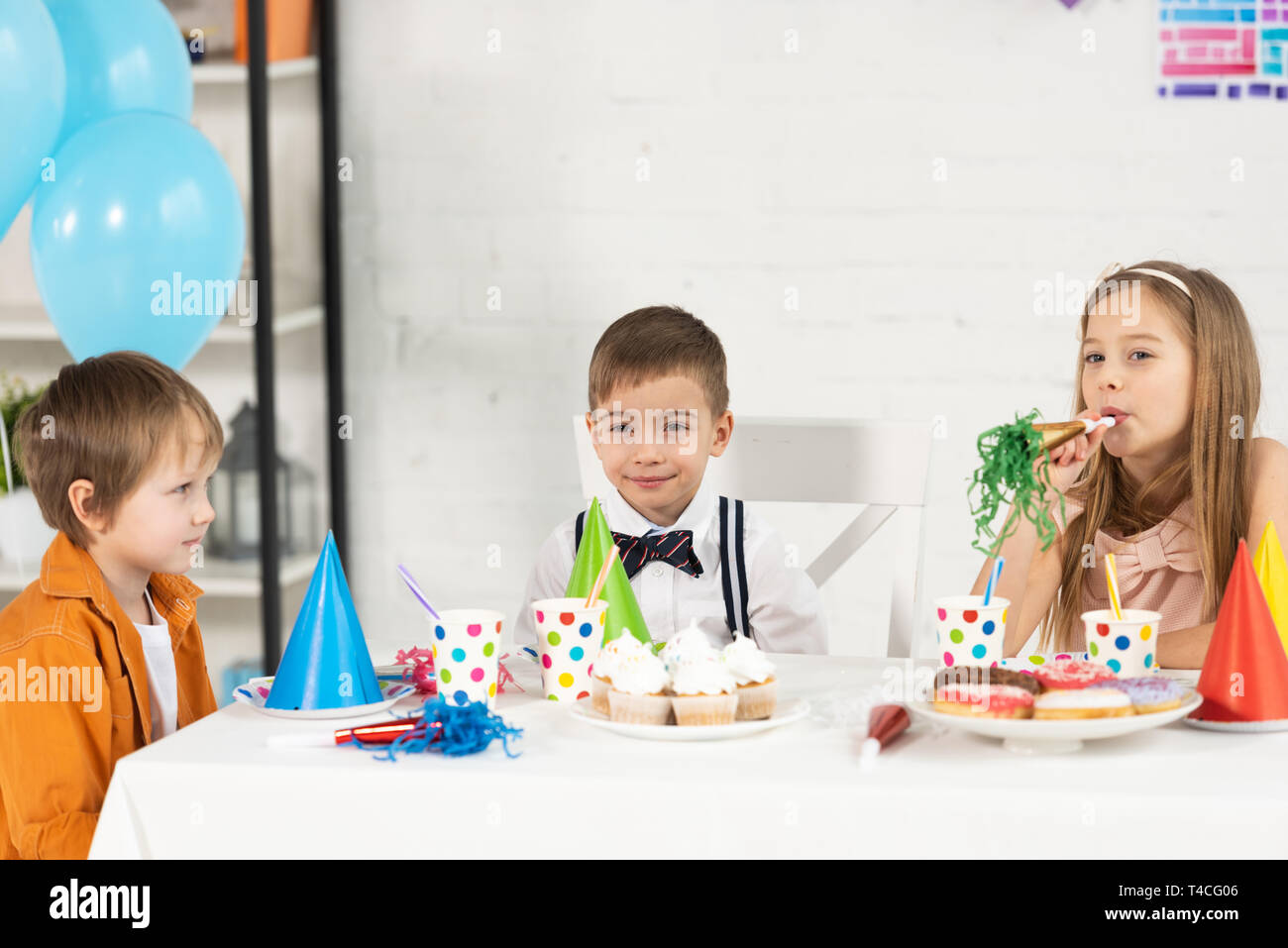 kids sitting at table with cupcakes and party horns during birthday ...