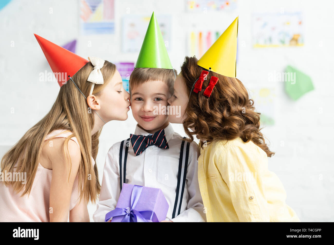 kids in party caps kissing on cheeks adorable boy with gift box during ...