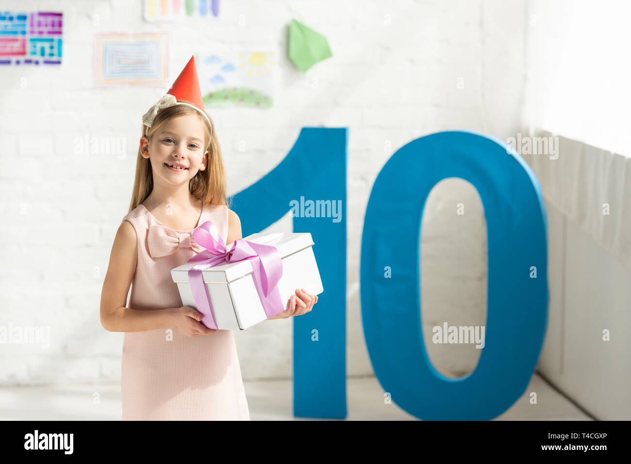 adorable happy kid in party cap holding present and posing near ...