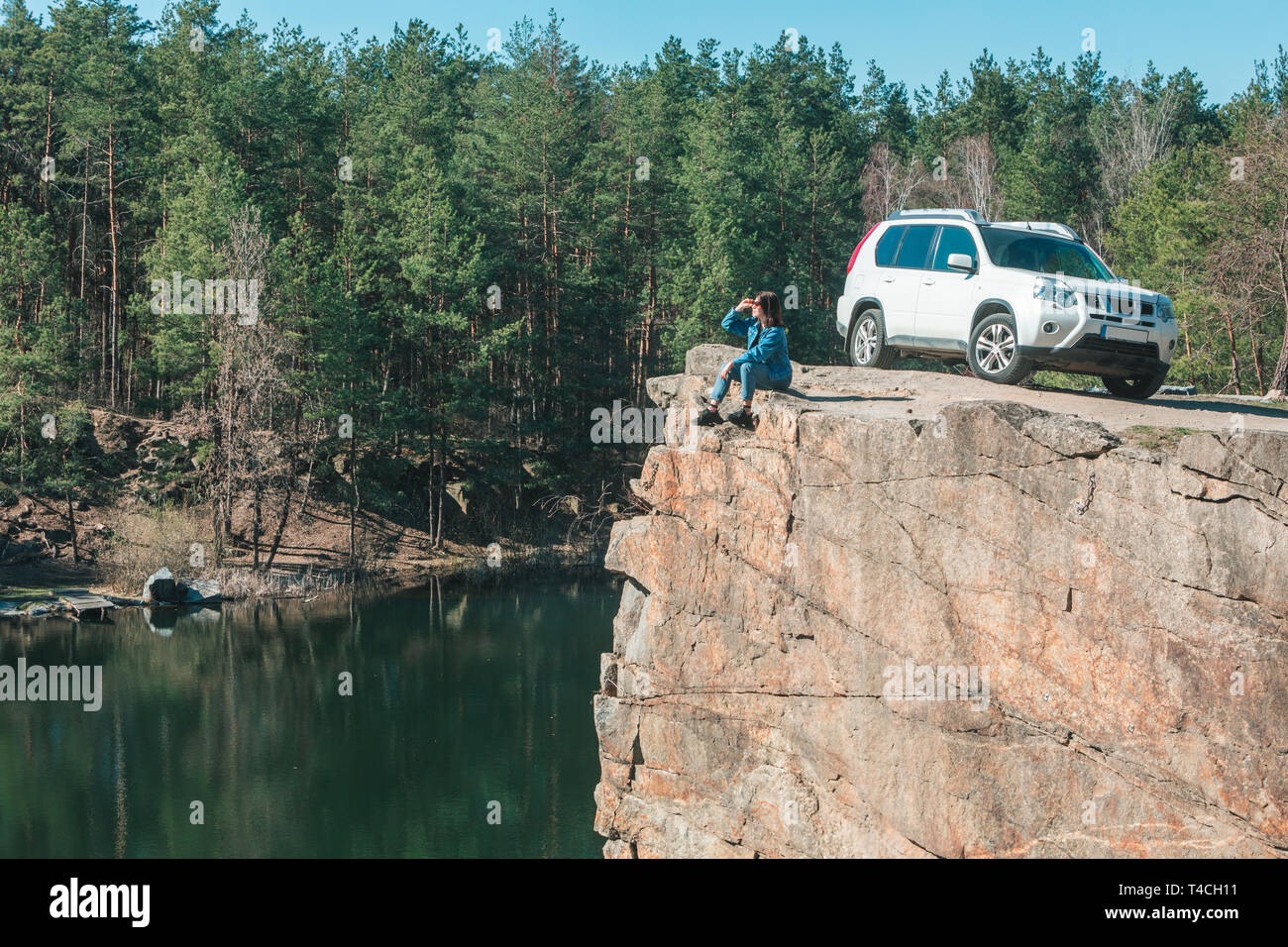 woman sitting on rocky edge with lake view. white suv car near. adventure concept Stock Photo ...