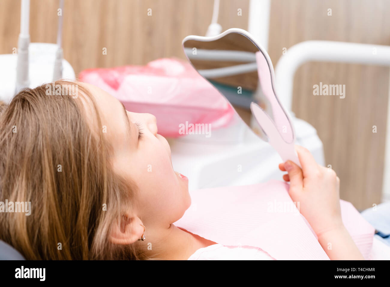Portrait of elementary age girl sitting in a dental chair inspecting ...