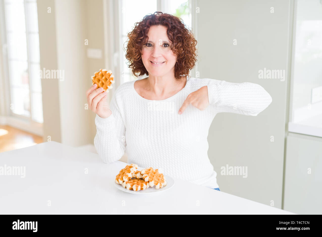 Senior woman eating sweet belgian waffle with surprise face pointing ...