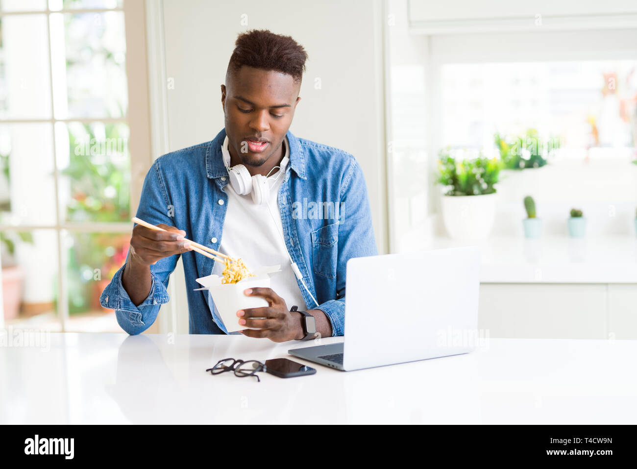 Handsome young african business man eating delivery asian food and ...