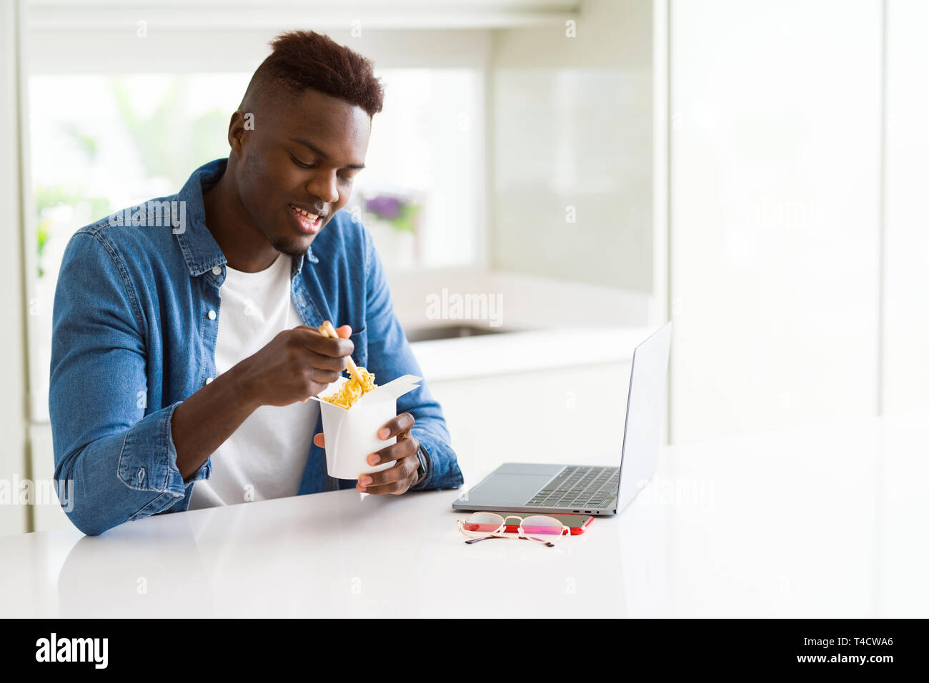Handsome young african business man eating delivery asian food and ...