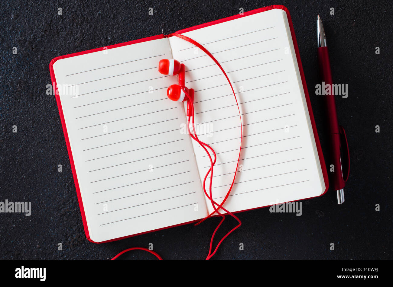Empty red notebook with red pen and headphones on dark background ...