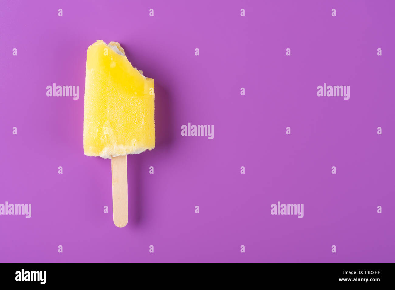 yellow popsicle with some bites on a purple background Stock Photo - Alamy